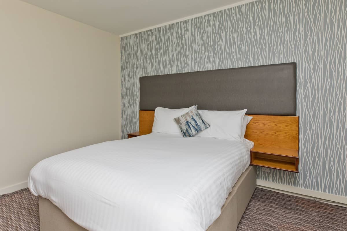 Cama bem arrumada com cabeceira de madeira e edredom branco.