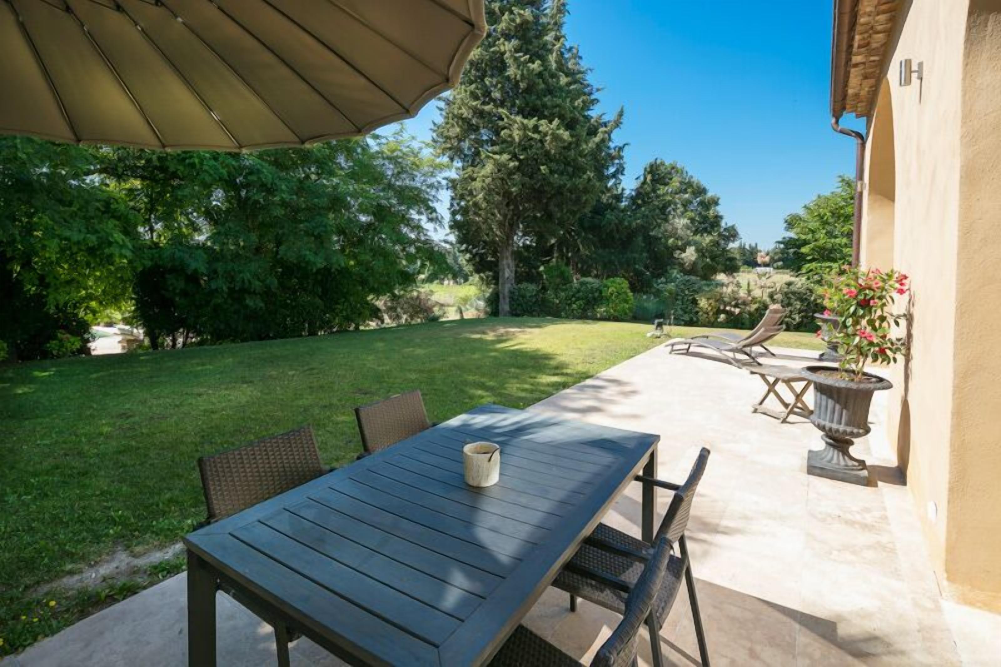 Um pátio com mesa, cadeiras, um guarda-sol grande e um vaso de planta.