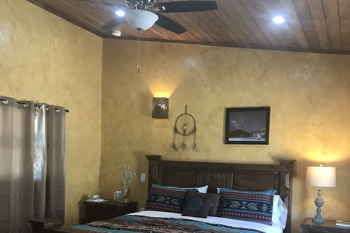 Quarto com teto de madeira, cama com roupa de cama estampada, luminária fixada na parede e ventoinha de teto.