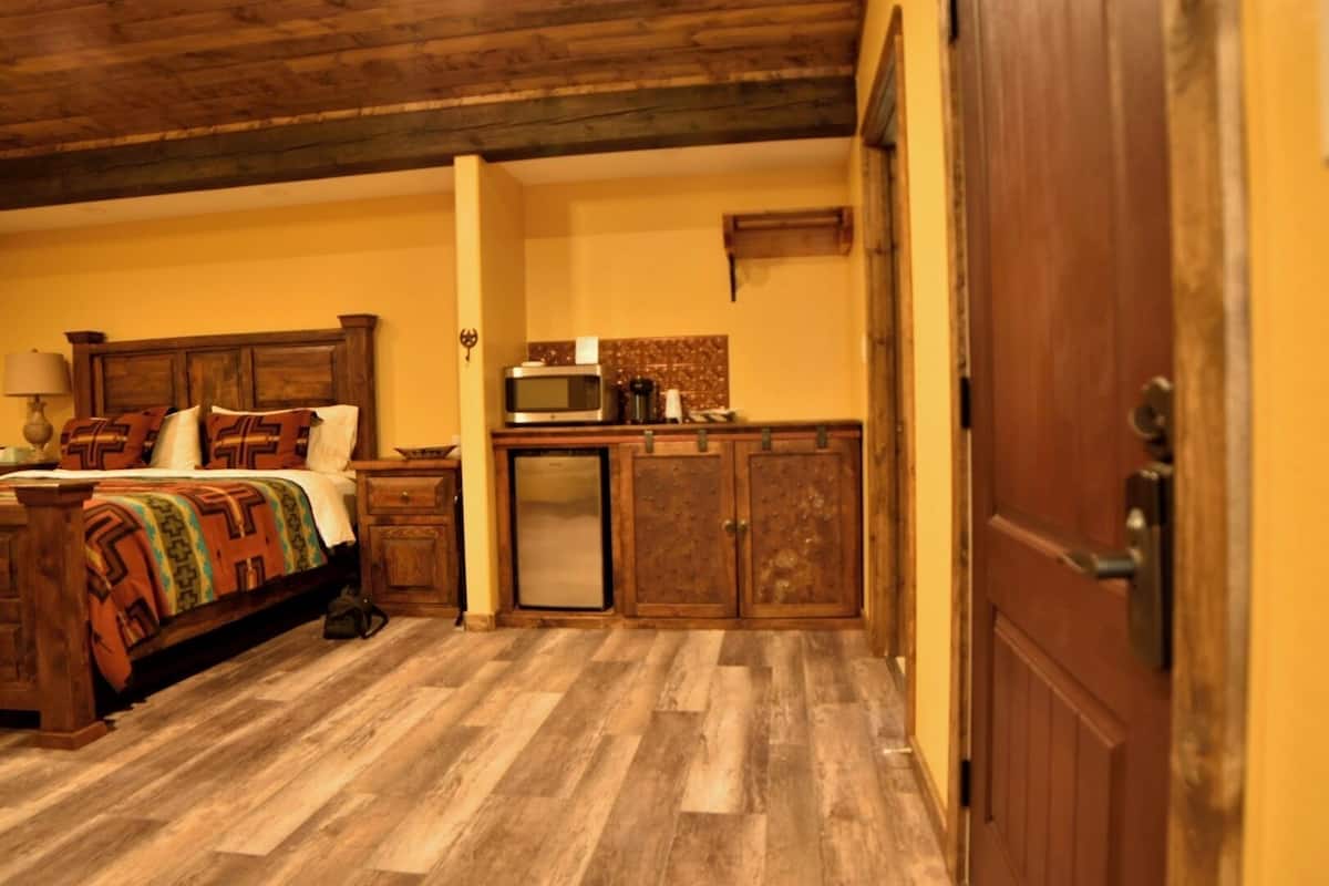 Quarto com cama de madeira, uma pequena cozinha e porta de madeira.