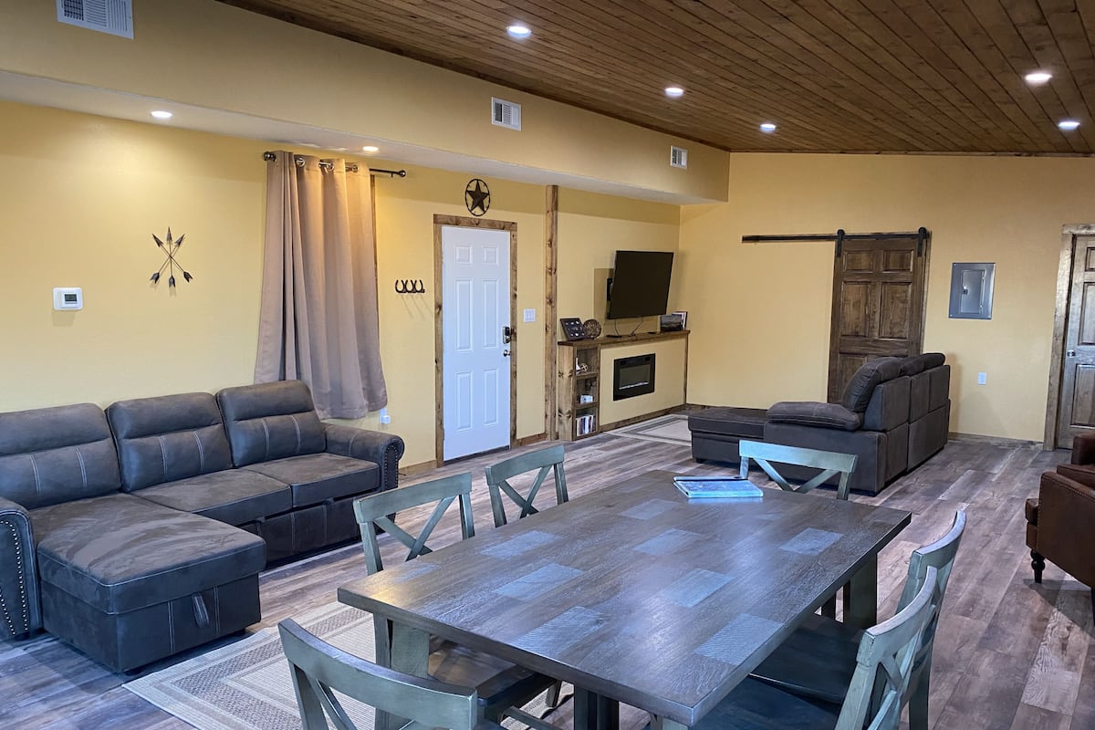 Uma sala de estar com teto de madeira, um sofá, uma mesa de jantar e uma lareira.