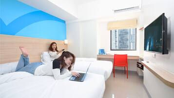 Quarto de hotel com cama, escrivaninha, cadeira, televisão e janela com vista para a cidade.