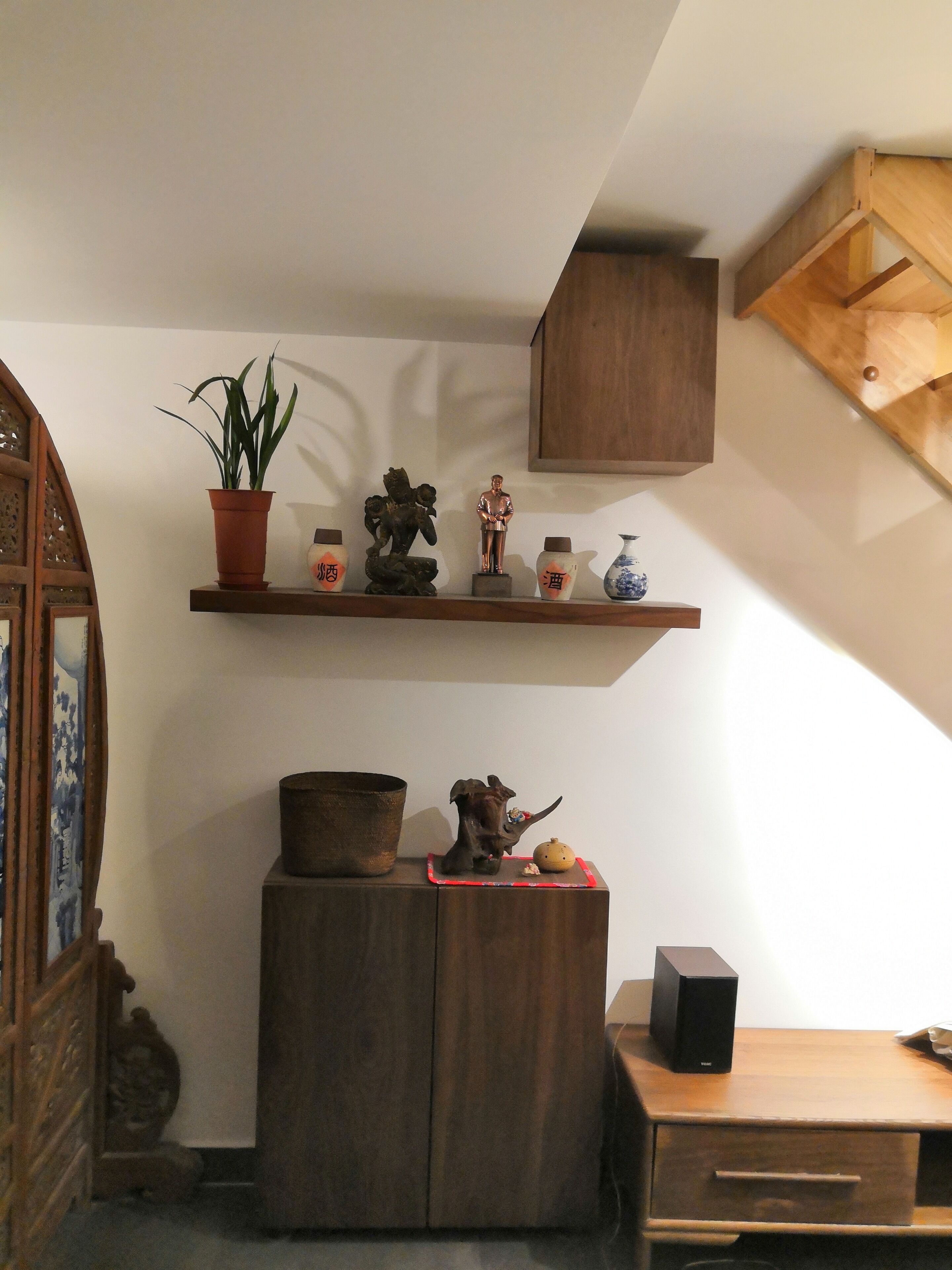 Quarto com um armário de madeira, uma estante com objetos decorativos, uma planta em vaso e um aparelho de som.