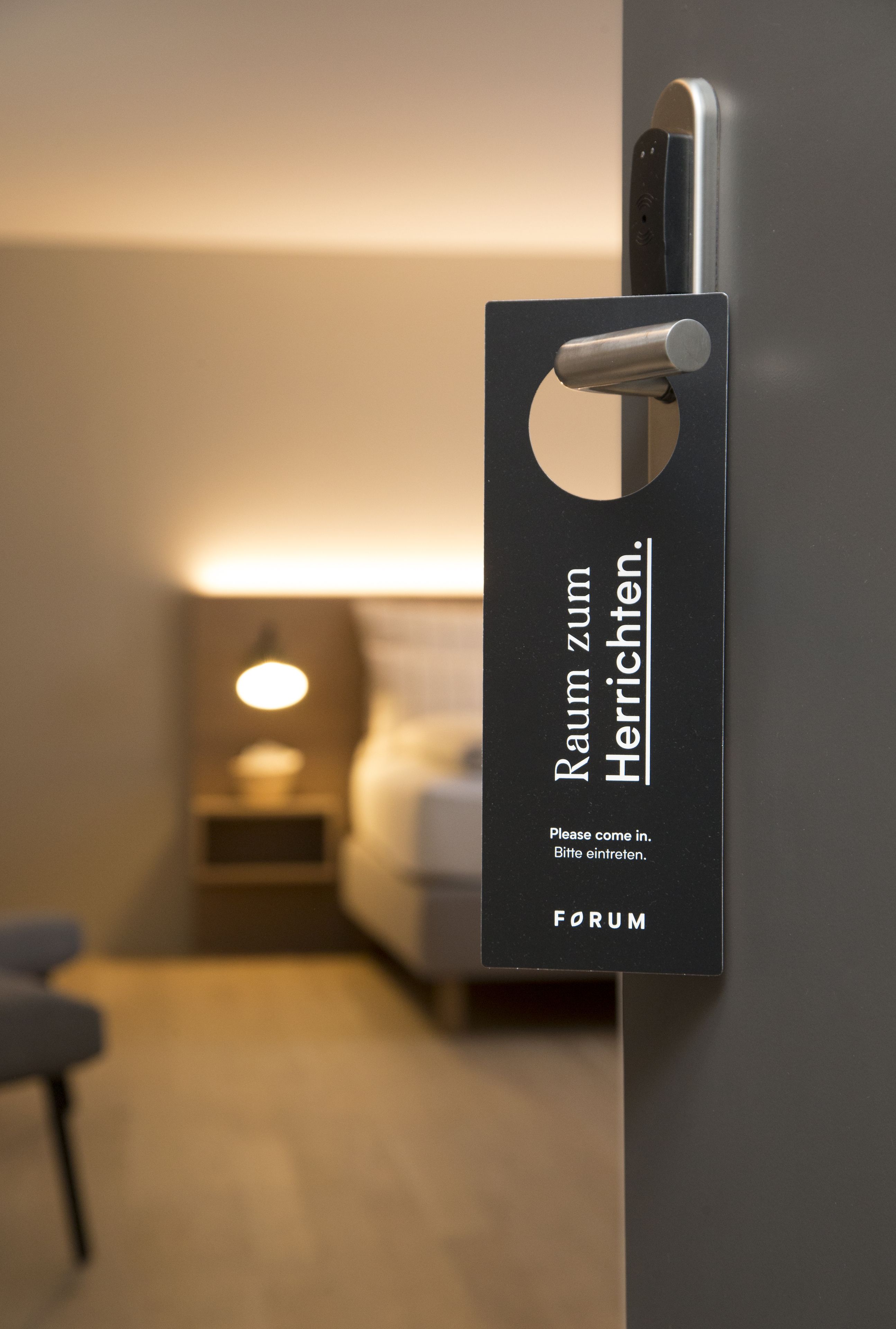Porta de quarto de hotel com um aviso que diz "Raum zum Herrichten. Please come in. Bitte eintreten." e "FORUM".