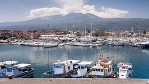 Uma marina com barcos atracados, montanhas ao fundo e uma cidade distante.
