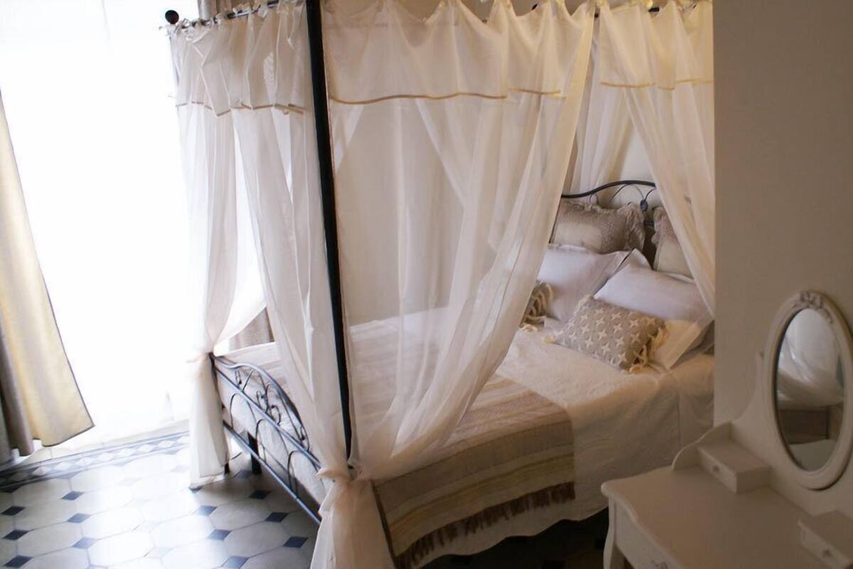 Quarto com cama de dossel, mesa de cabeceira e espelho.