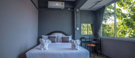 Cama bem arrumada com lençóis e almofadas brancos, mesa de cabeceira com uma cadeira e uma janela com cortinas.