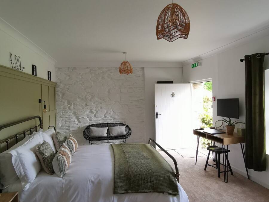 Quarto com cama, escrivaninha e cadeira. Parede branca com textura, luminária pendente de vime e porta com puxador verde.