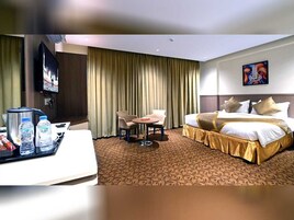 Quarto de hotel com uma cama, uma escrivaninha com cafeteira e garrafas de água, uma cadeira e uma televisão.