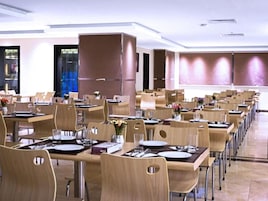 Uma sala de jantar moderna com várias mesas e cadeiras, com louças preparadas e um elemento decorativo central.