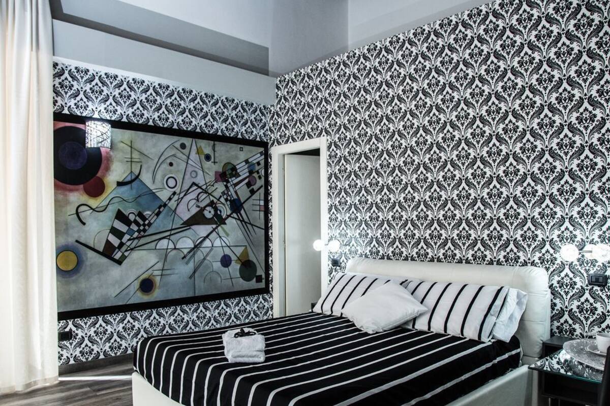 Quarto moderno com cama grande, parede decorativa com padrão em preto e branco e uma grande pintura abstrata.