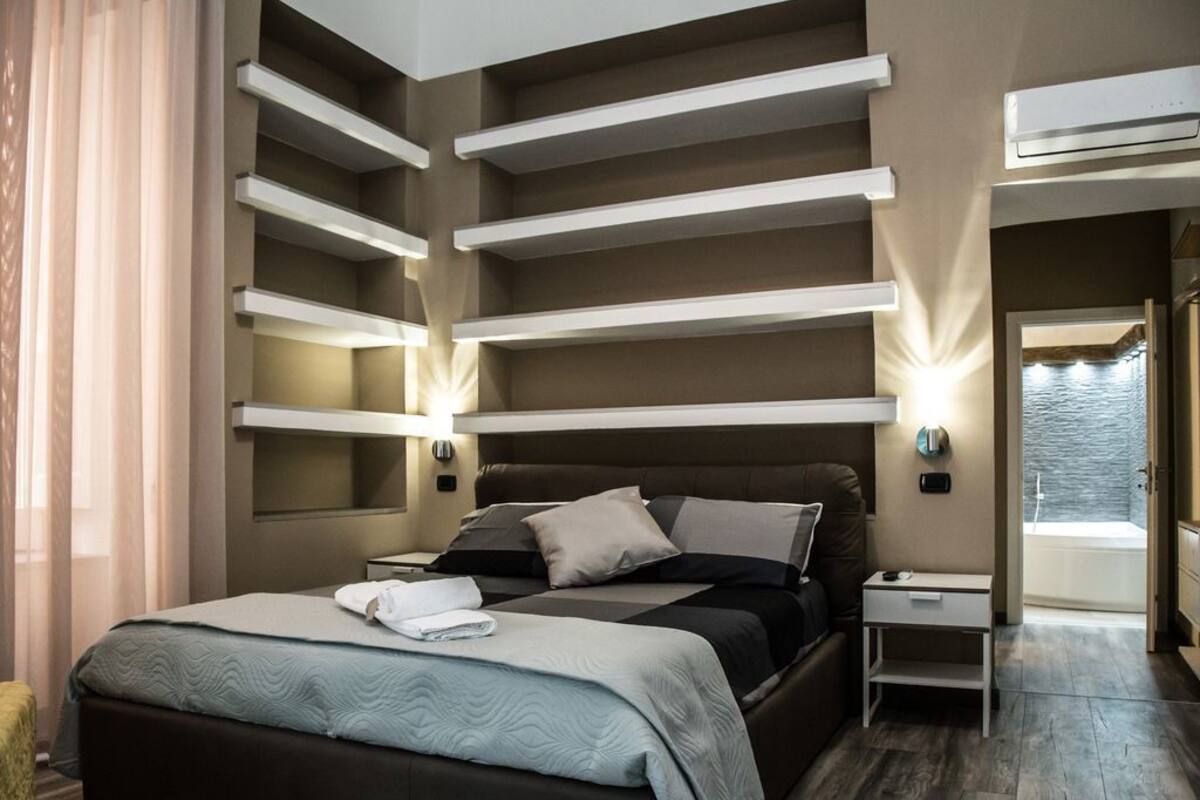Quarto de hotel moderno com uma cama grande, estantes embutidas e vista para a água.