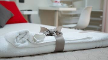 Cama bem arrumada com uma toalha branca dobrada e uma fita cinza.