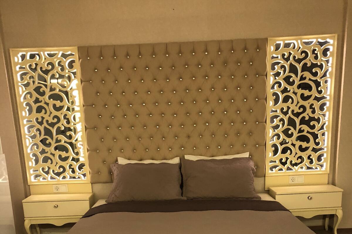 Uma cama grande com cabeceira estofada, duas mesas de cabeceira e painéis decorativos em ambos os lados.
