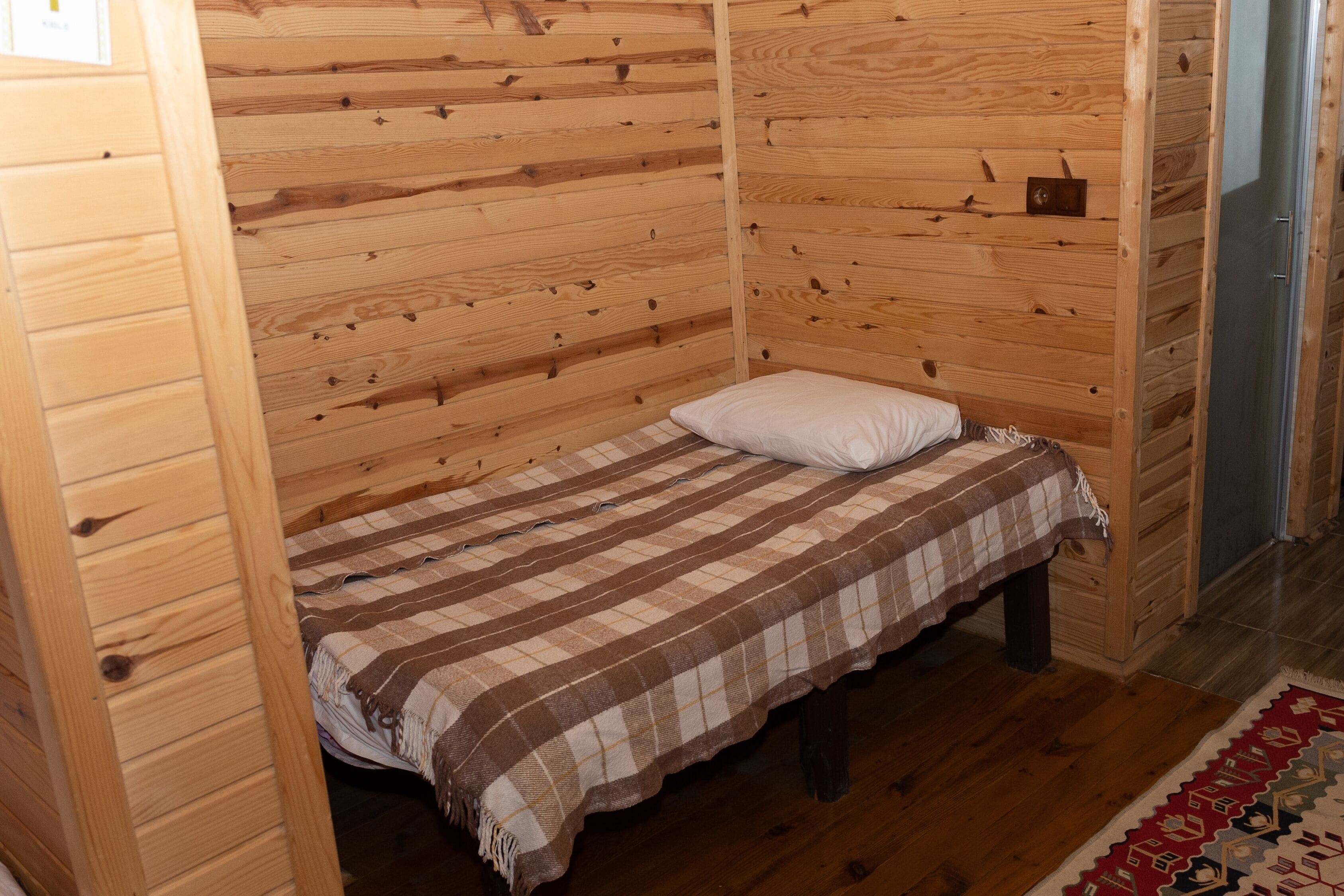 Um quarto de cabana de madeira, com uma cama de solteiro, um guarda-roupa de madeira e uma pequena mesa.