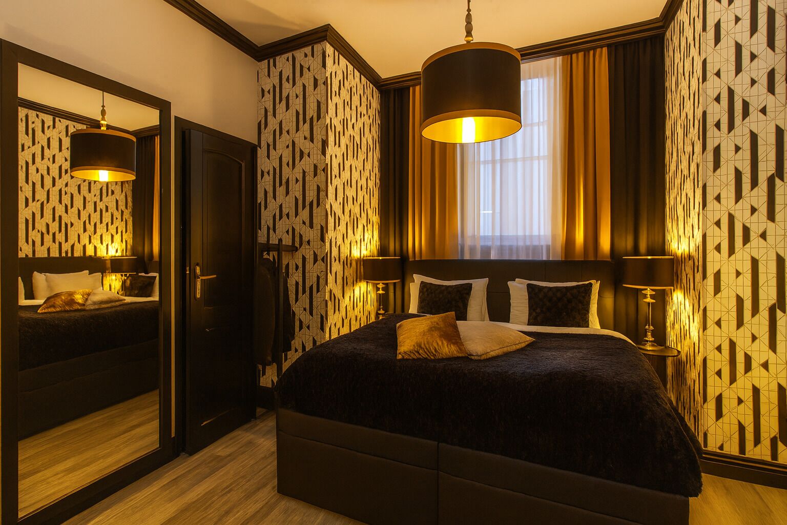 Quarto moderno com cama grande, soalho de madeira escura, papel de parede estampado e iluminação ambiente.
