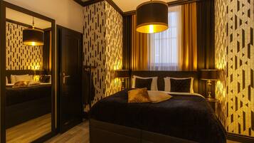 Quarto moderno com cama grande, soalho de madeira escura, papel de parede estampado e iluminação ambiente.