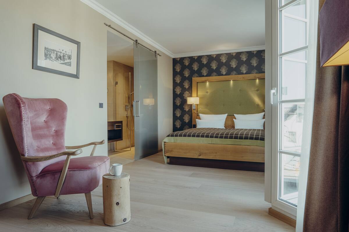 Quarto de hotel moderno com cama, uma cadeira, mesa de cabeceira e área de chuveiro.