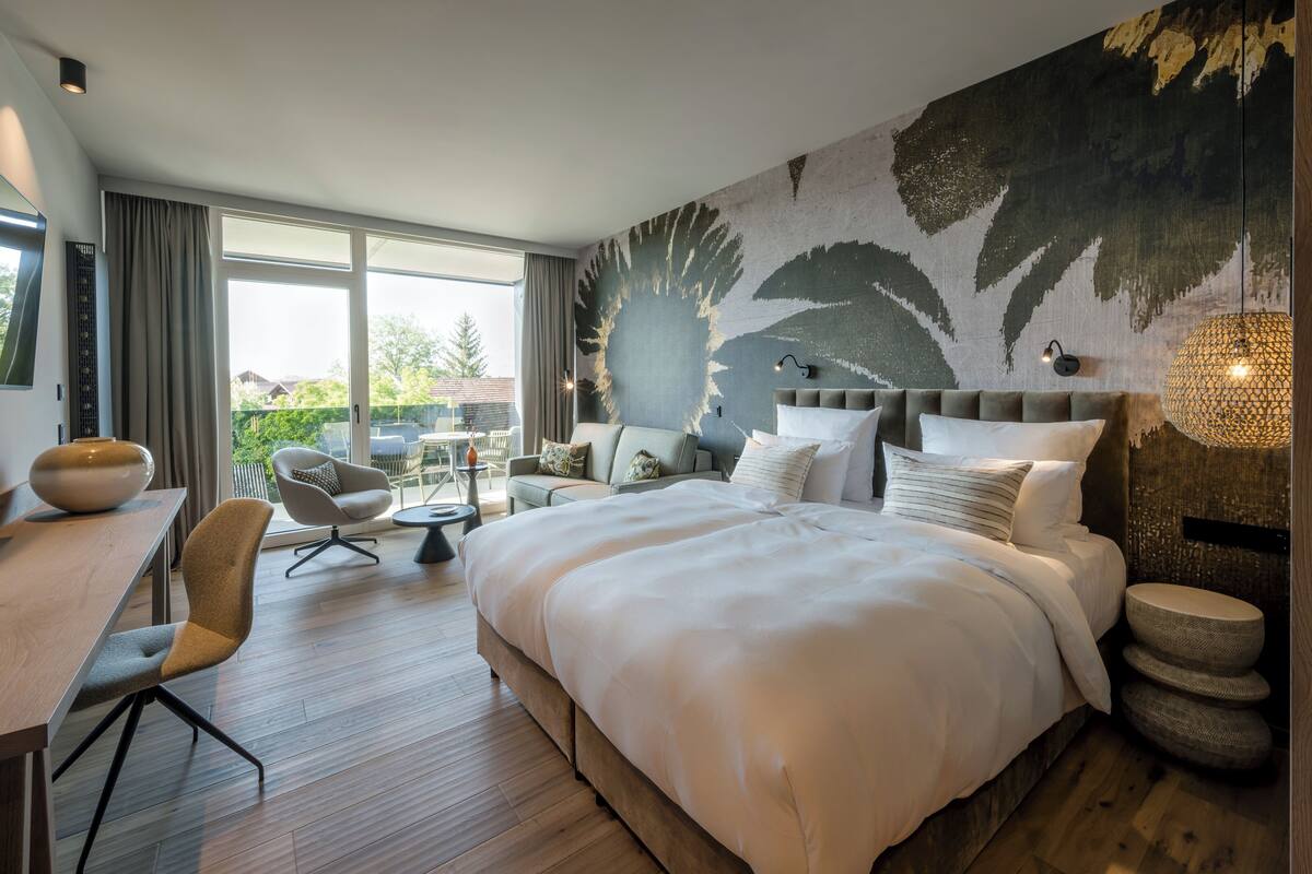Quarto de hotel moderno com uma cama grande, uma escrivaninha, uma cadeira e vista para o exterior.