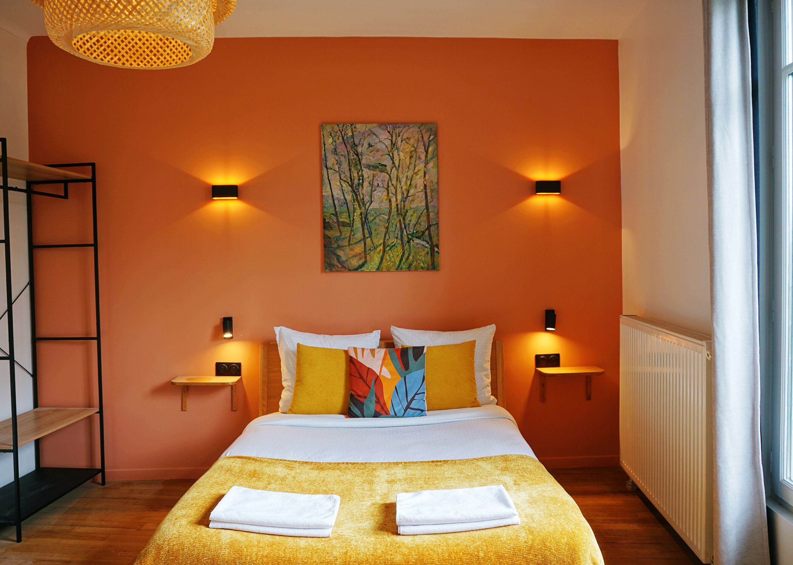 Quarto de hotel com uma cama, duas mesas de cabeceira, um quadro na parede e uma janela com cortinas.