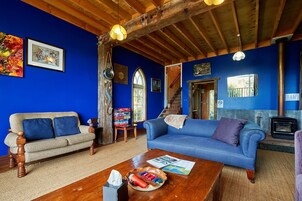 Uma sala de estar acolhedora com paredes azuis, vigas de madeira, uma lareira e uma escada que leva a outro andar.