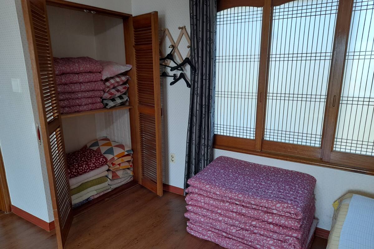 Quarto com guarda-roupa de madeira, cama com colcha floral e janela com padrão quadriculado.