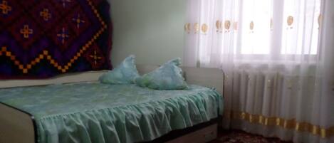 Um quarto com uma cama, uma janela com cortinas e um cobertor estampado na parede.