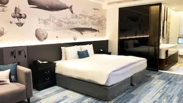 Quarto de hotel moderno com uma cama grande, mesa de cabeceira, uma cadeira e um mural na parede.