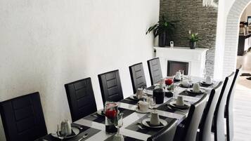 Uma área de jantar moderna com uma mesa comprida posta para seis pessoas, cadeiras pretas e uma parede de pedra com lareira.