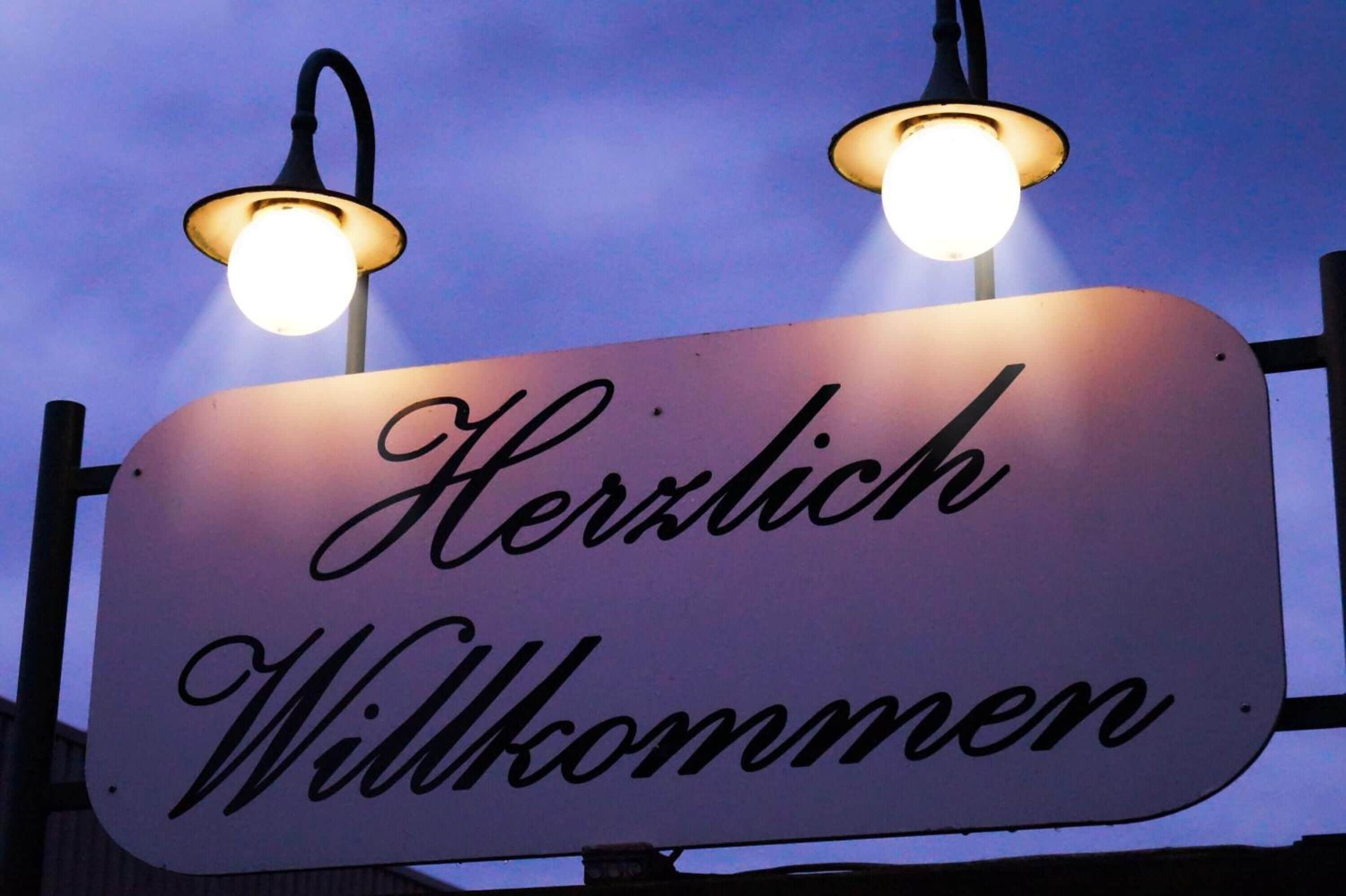 Uma placa com a inscrição 'Herzlich Willkommen' iluminada por duas luzes.