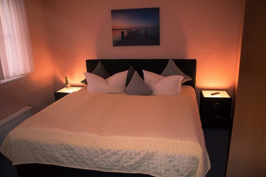 Cama bem arrumada com manta acolchoada, cabeceira com padrões geométricos e um quadro de um cais na parede.
