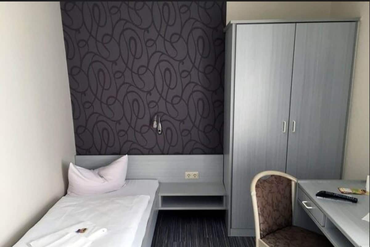 Quarto de hotel com cama, escrivaninha, cadeira e guarda-roupa.