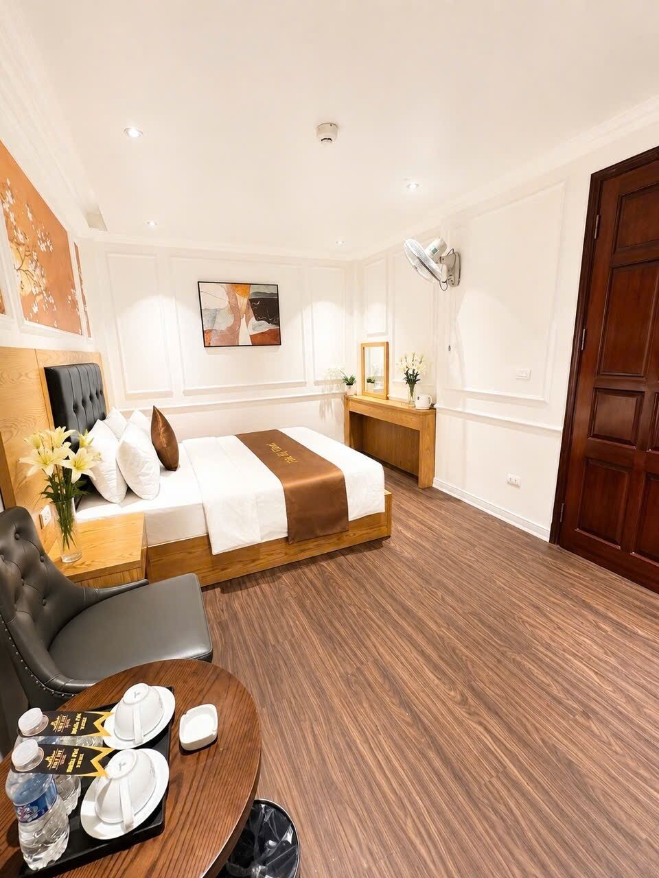 Quarto de hotel com uma cama, uma escrivaninha, uma cadeira e uma mesa com um tabuleiro de pratos e uma garrafa de água.