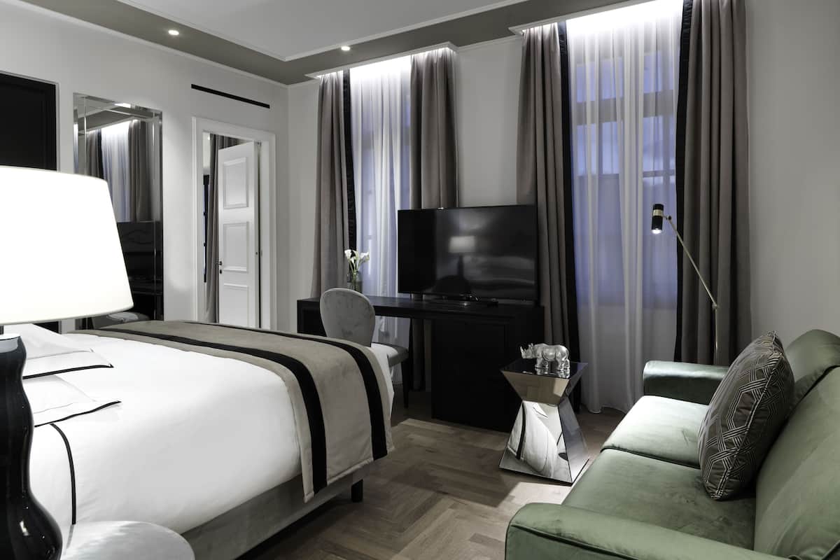 Quarto de hotel moderno com uma cama grande, uma escrivaninha com televisão de tela plana, um sofá verde e um abajur.