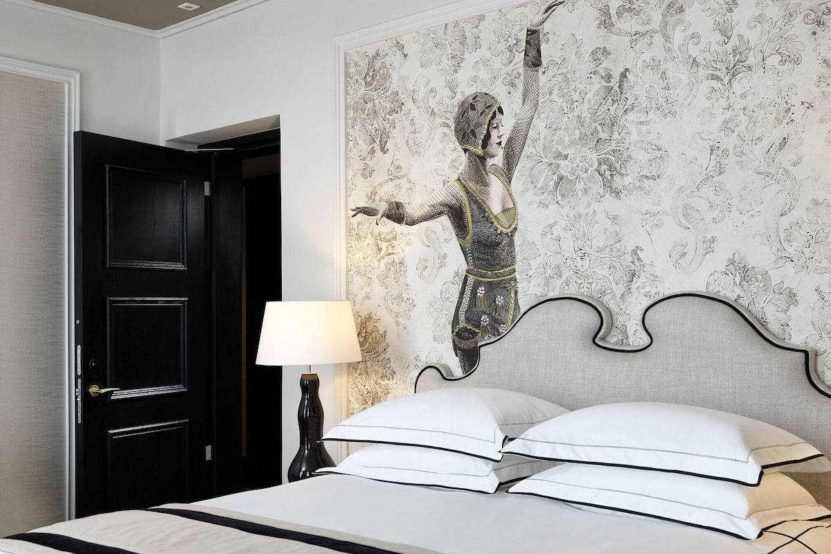 Quarto de hotel com cama, porta preta, parede com padrão floral e luminária.