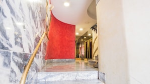 Uma escadaria de mármore com uma parede de destaque vermelha e um corrimão dourado que leva a um espaço interior moderno.
