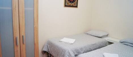 Quarto com duas camas de solteiro, um guarda-roupa e um quadro na parede.