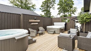 Um deck de madeira com hidromassagem, móveis de vime e espaço para churrasco.