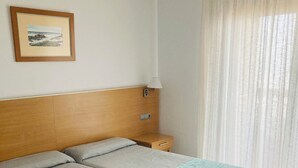 Uma cama de casal com colcha cinza e verde-água, uma cabeceira de madeira, uma mesa de cabeceira com abajur e um quadro emoldurado na parede.