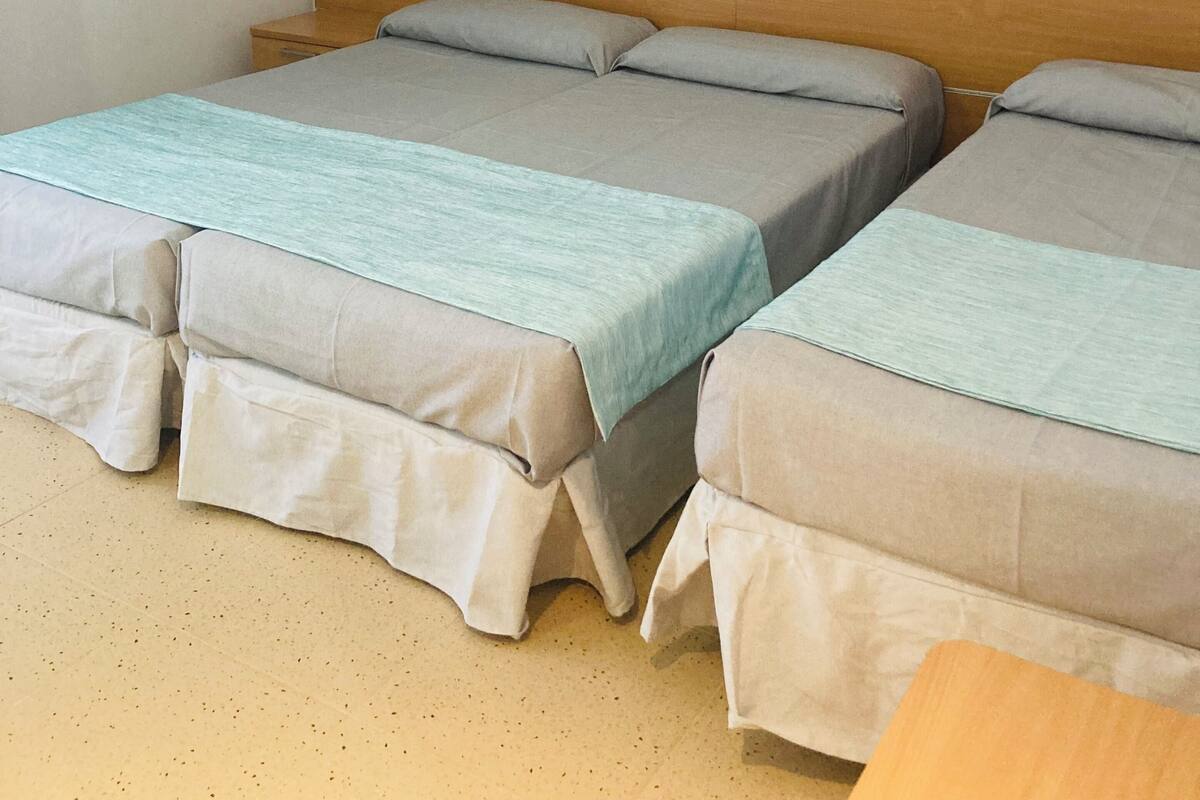 Quarto de hotel com duas camas, cabeceira de madeira, mesa de cabeceira, luminária e um quadro na parede.