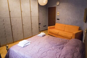 Um quarto com uma cama, um sofá laranja, um guarda-roupa e um relógio na parede.
