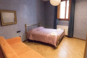 Quarto com cama, janela com cortinas, radiador e quadro na parede.