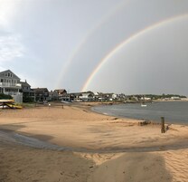 Uma praia com casas ao fundo e um arco-íris no céu.