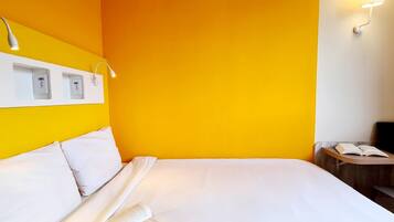 Quarto de hotel com cama, mesa de cabeceira, luminária na parede e tomada.