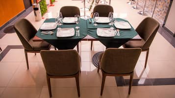Uma sala de jantar com quatro mesas preparadas para quatro pessoas, cada uma com cadeiras, pratos, talheres e copos.