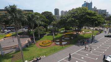 Um parque urbano com um canteiro de flores circular, palmeiras e um estacionamento.
