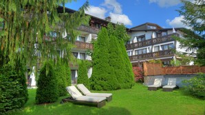 Um hotel de vários andares com varandas, um jardim bem cuidado e espreguiçadeiras.