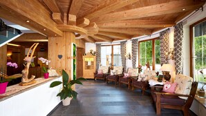 Interior em madeira com balcão de recepção, área de estar e grandes janelas.