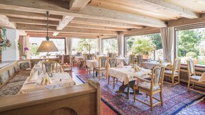 Restaurante com vigas de madeira, mesas com toalhas brancas e um tapete estampado.