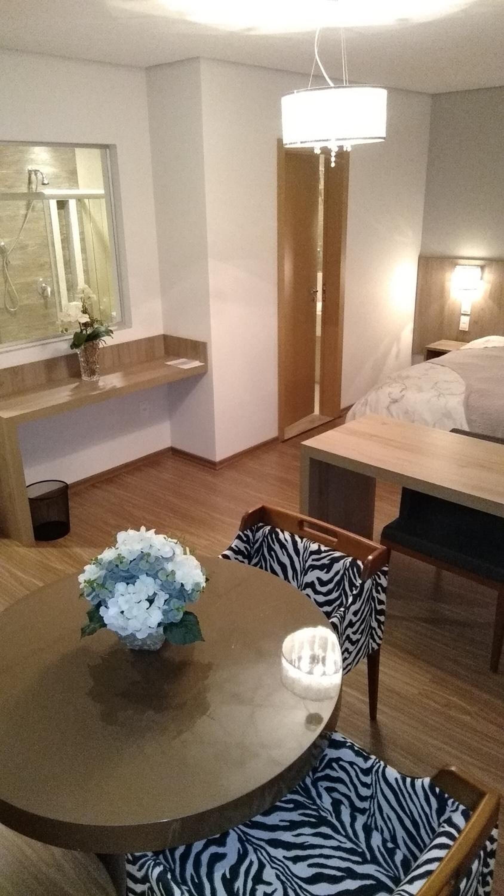 Quarto de hotel com área de refeições, cama, mesa de cabeceira, janela com vista e uma pequena planta na mesa.